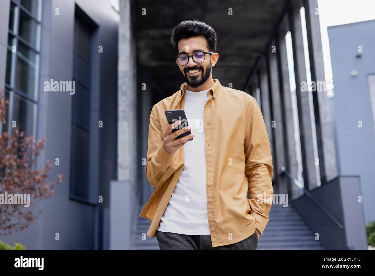 A young smiling man walks through the city with a phone in his hands ...