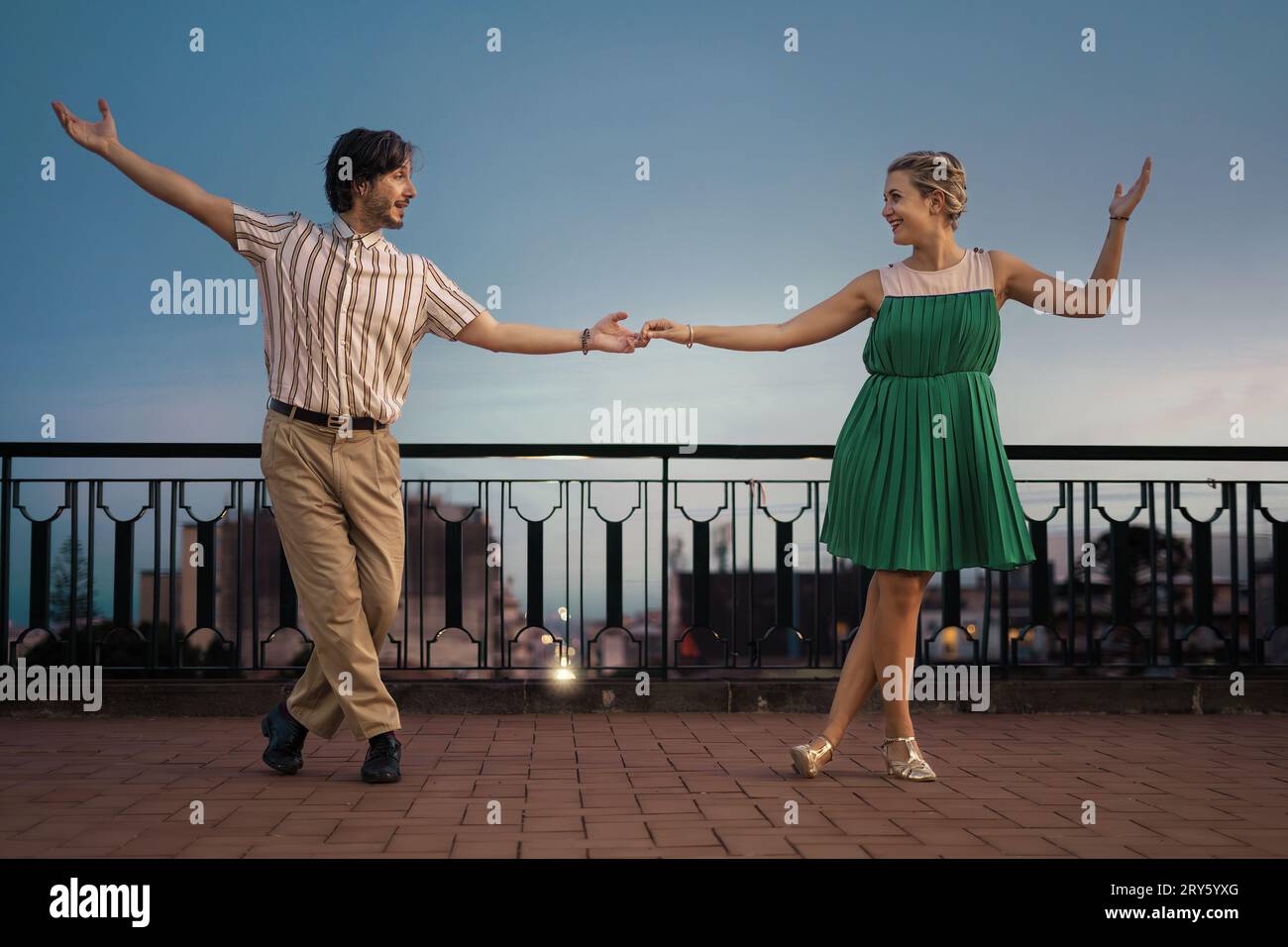 Couple swing dancing on a terrace, captured in profile as they hold ...