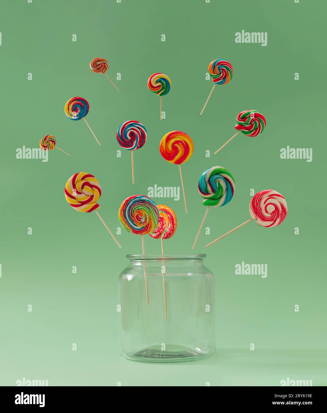 Colorful lollipops coming out of jar against pastel green background ...