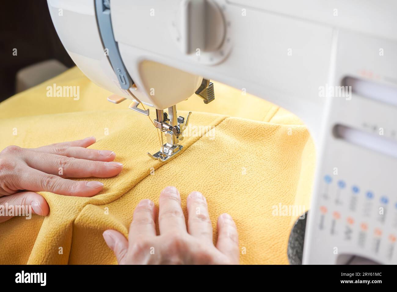Tailor hands stitching yellow fabric on modern sewing machine at workplace in atelier. Women's ...
