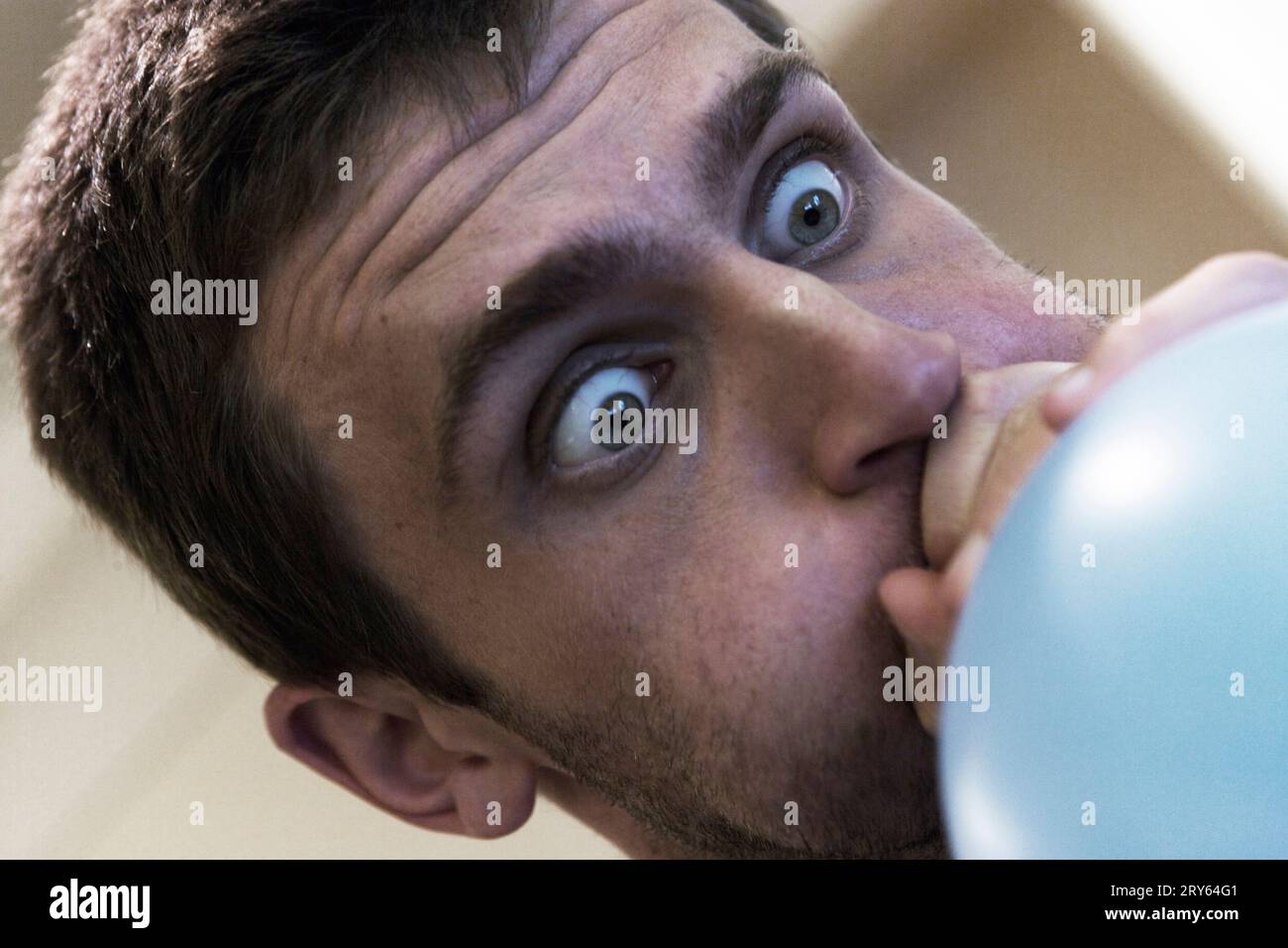 A young man with bulging eyes blowing up a blue balloon Stock Photo - Alamy