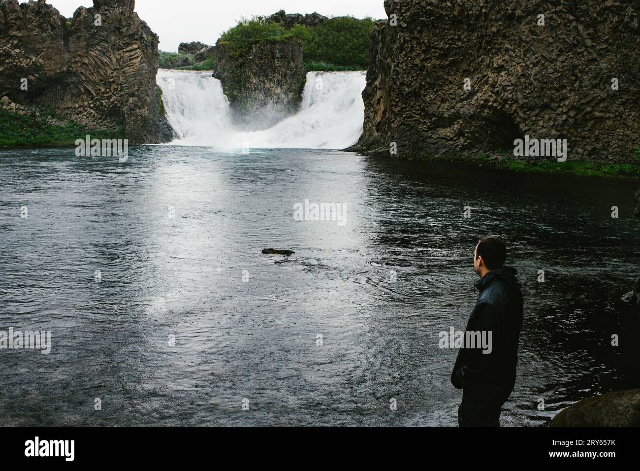 Man stands by pool of clear glacial water from waterfall Stock Photo ...