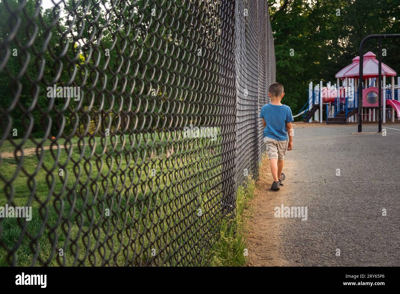 Young boy walking alongside fence at playground Stock Photo - Alamy