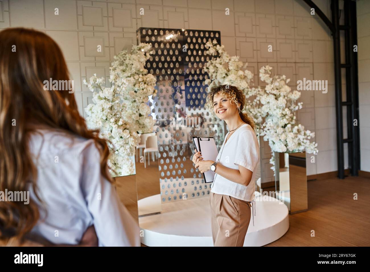 smiling decorator with clipboard showing white floral decor to enamored ...