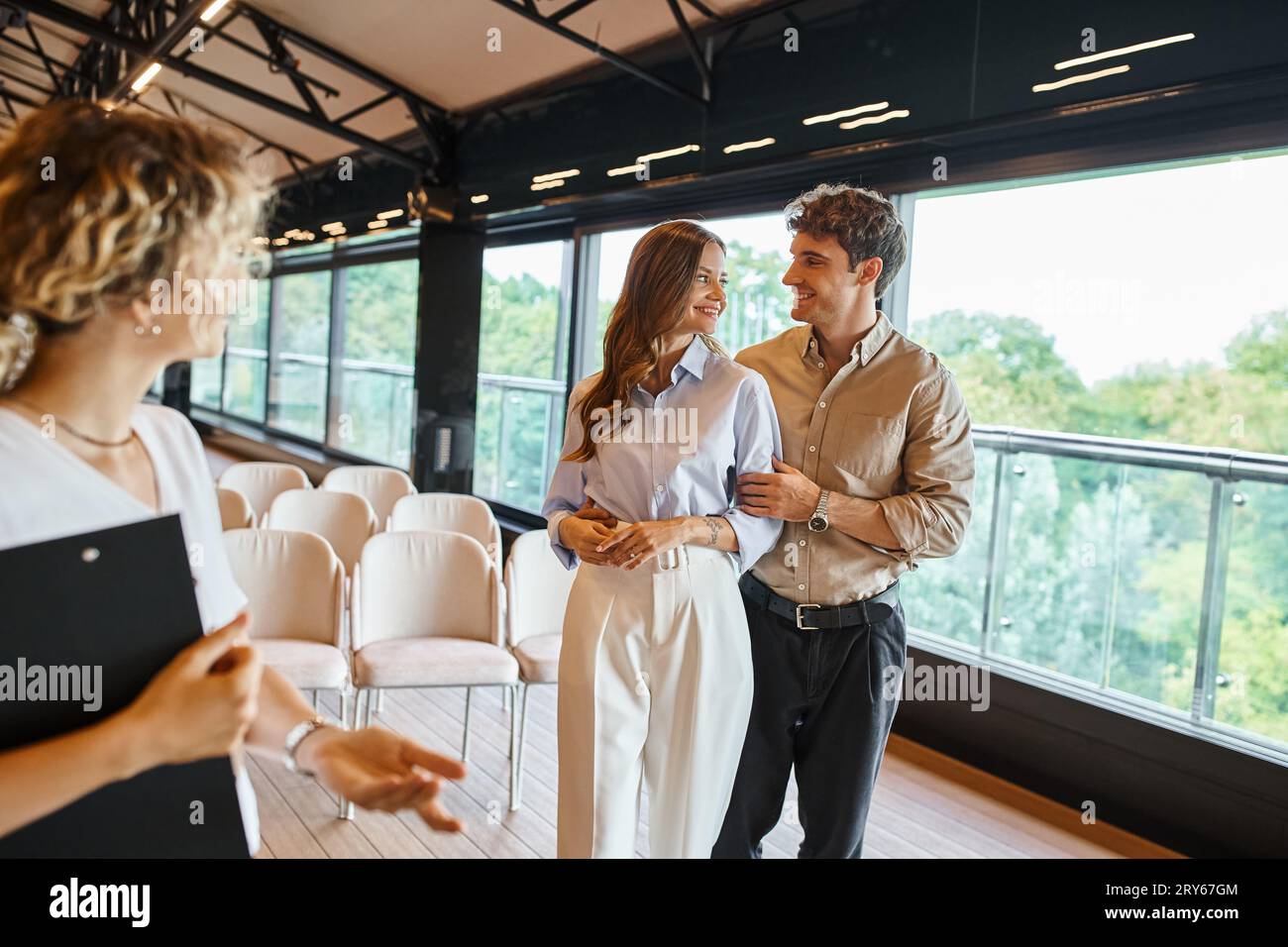 joyful couple smiling at each other near banquet coordinator with ...