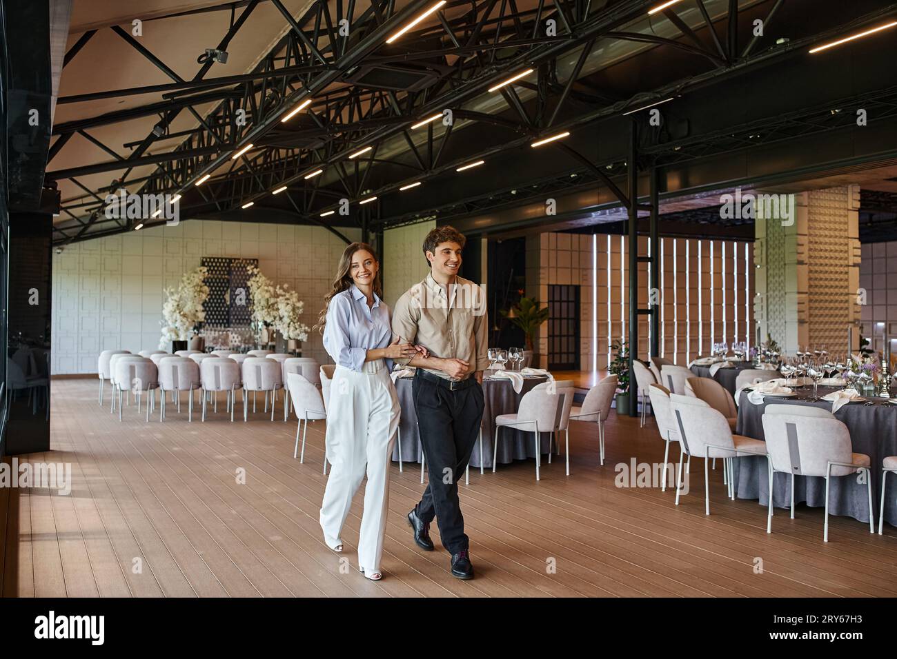 joyful couple walking along festive tables in modern spacious banquet ...