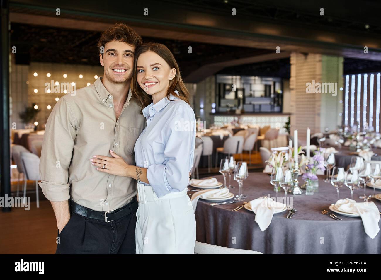 happy couple in love looking at camera in banquet hall with decorated ...