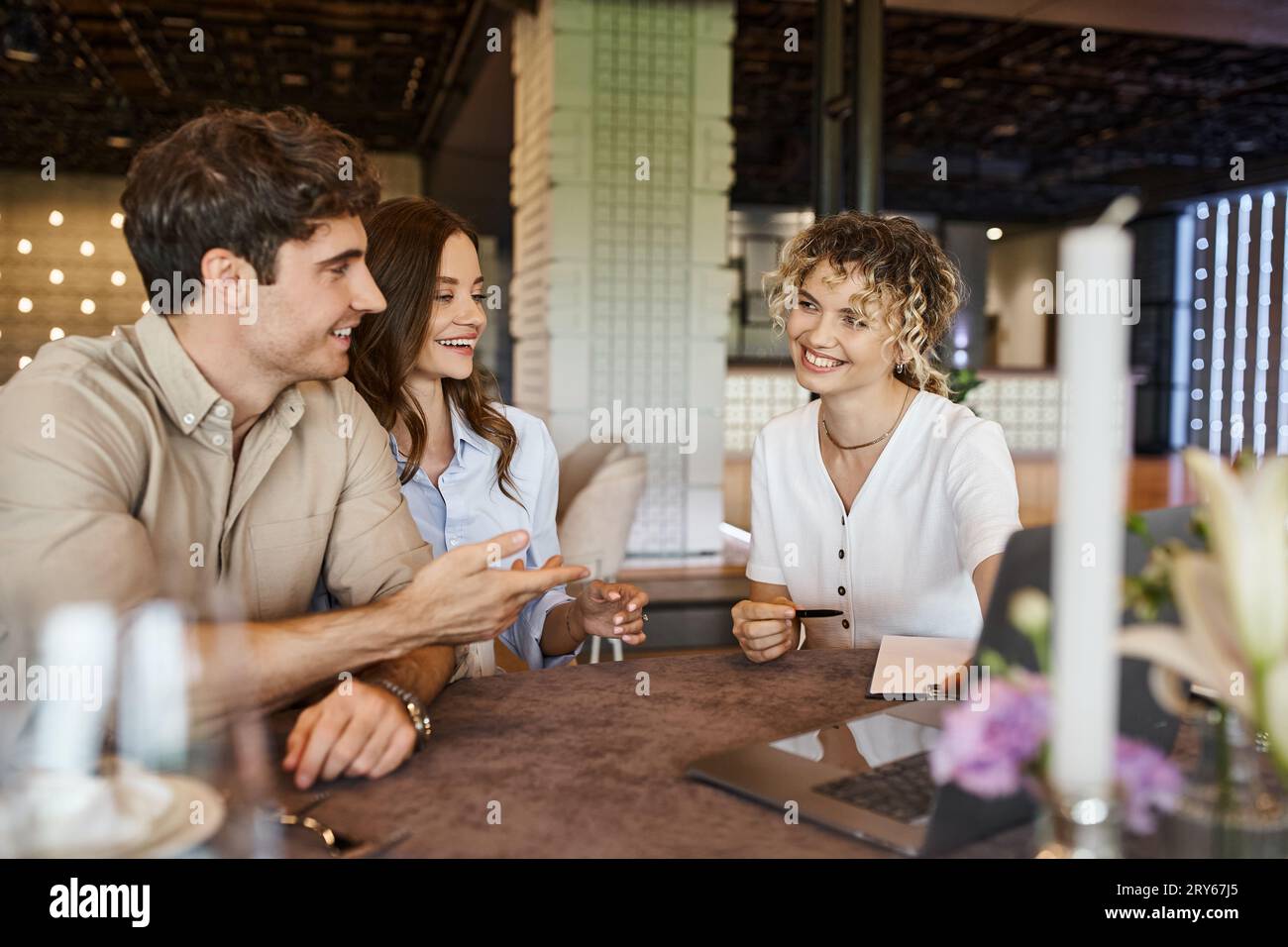 smiling man talking to event manager near happy girlfriend in banquet ...