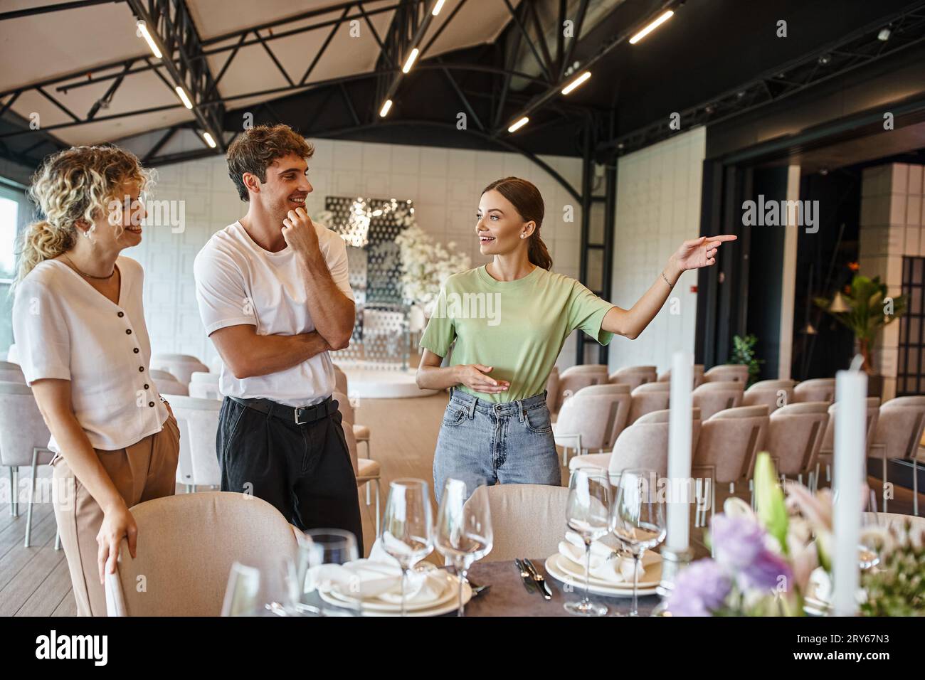 joyful team lead pointing with finger near event managers and festive ...