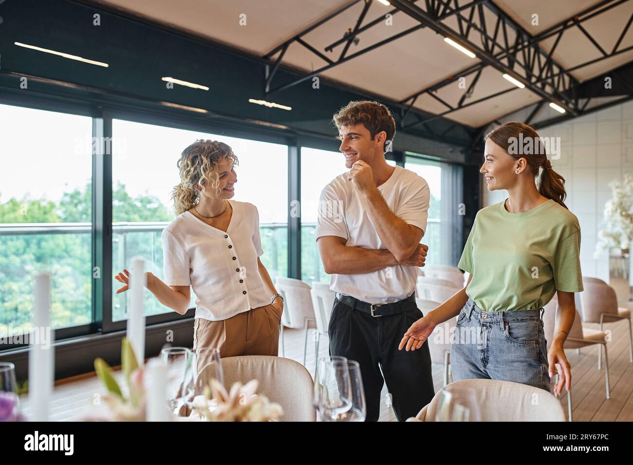 happy team of decorators talking near table with festive setting in ...