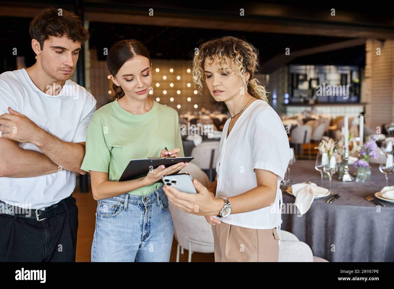 young woman writing notes on clipboard near colleague and team lead in ...