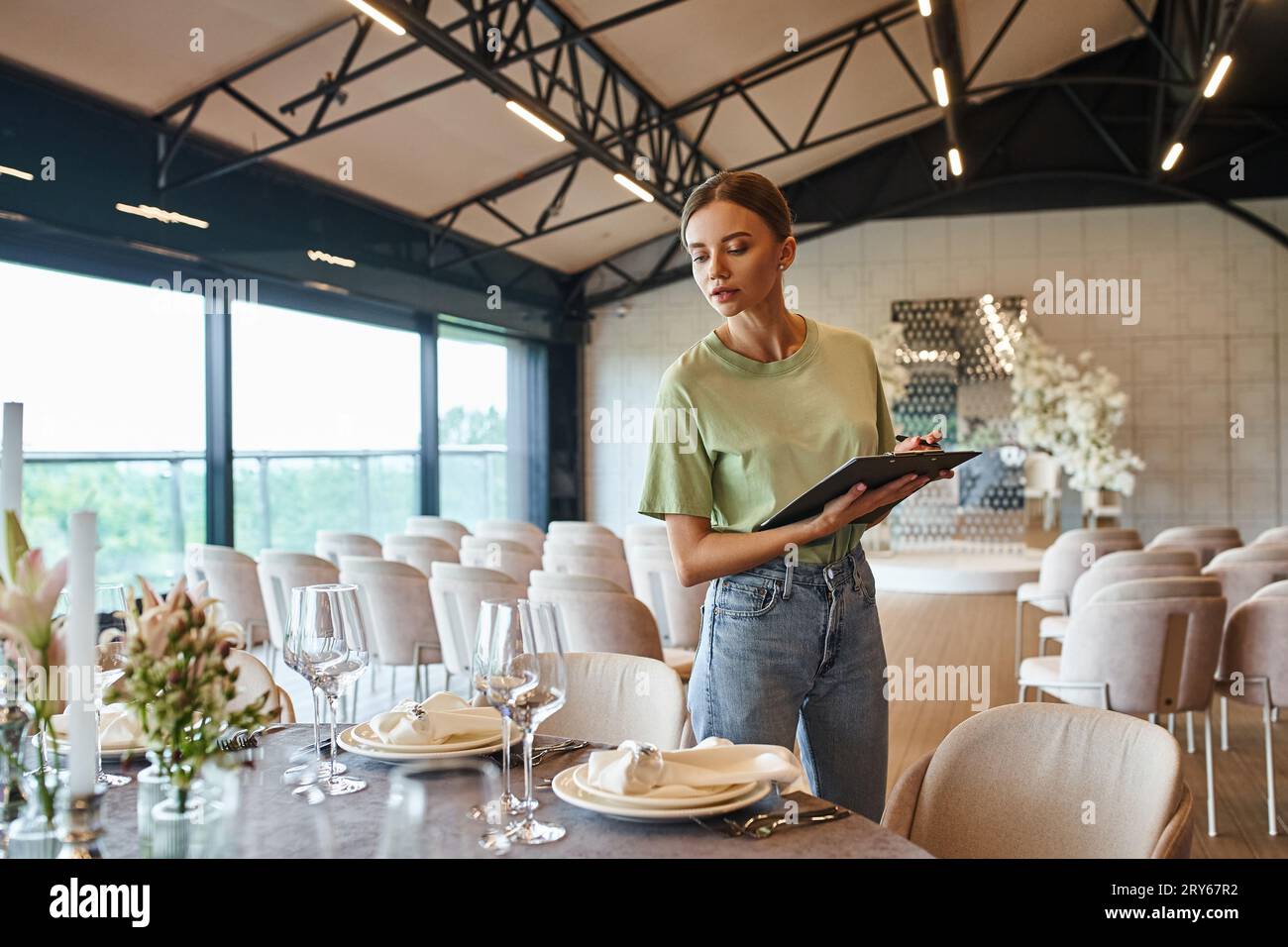 young female decorator with clipboard near table with banquet setting ...