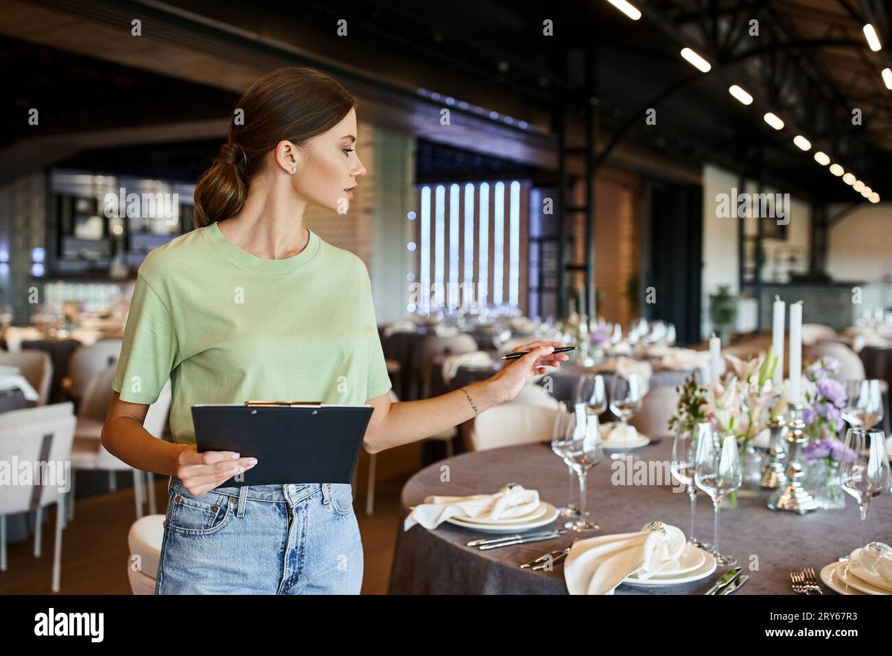 event manager holding clipboard and pointing with pen at table with ...