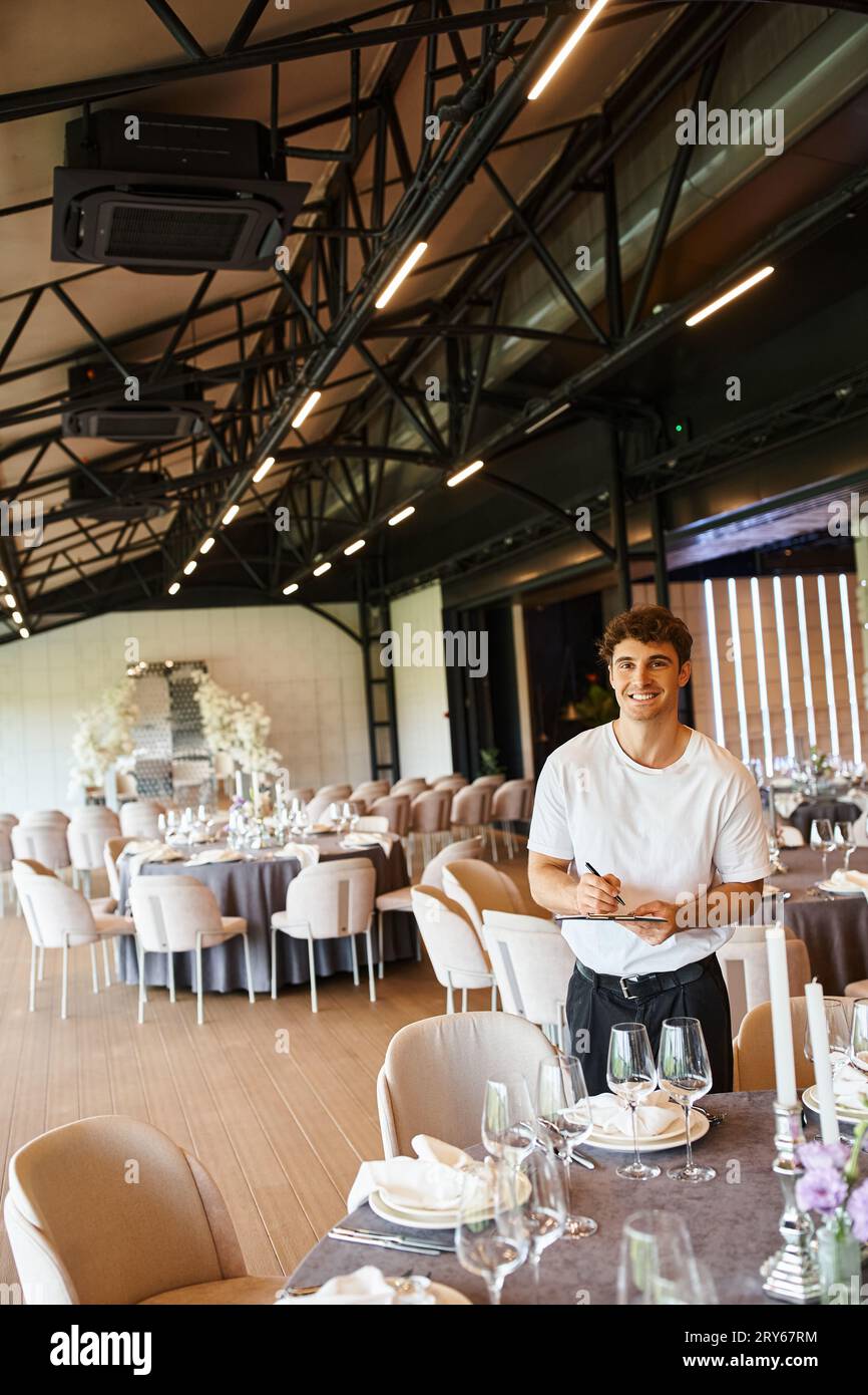 smiley event manager with clipboard looking at camera in modern banquet ...