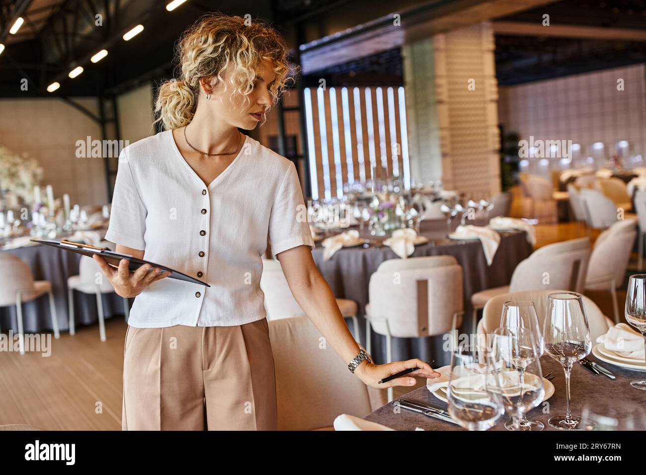 banquet coordinator with clipboard checking festive setting on table in ...