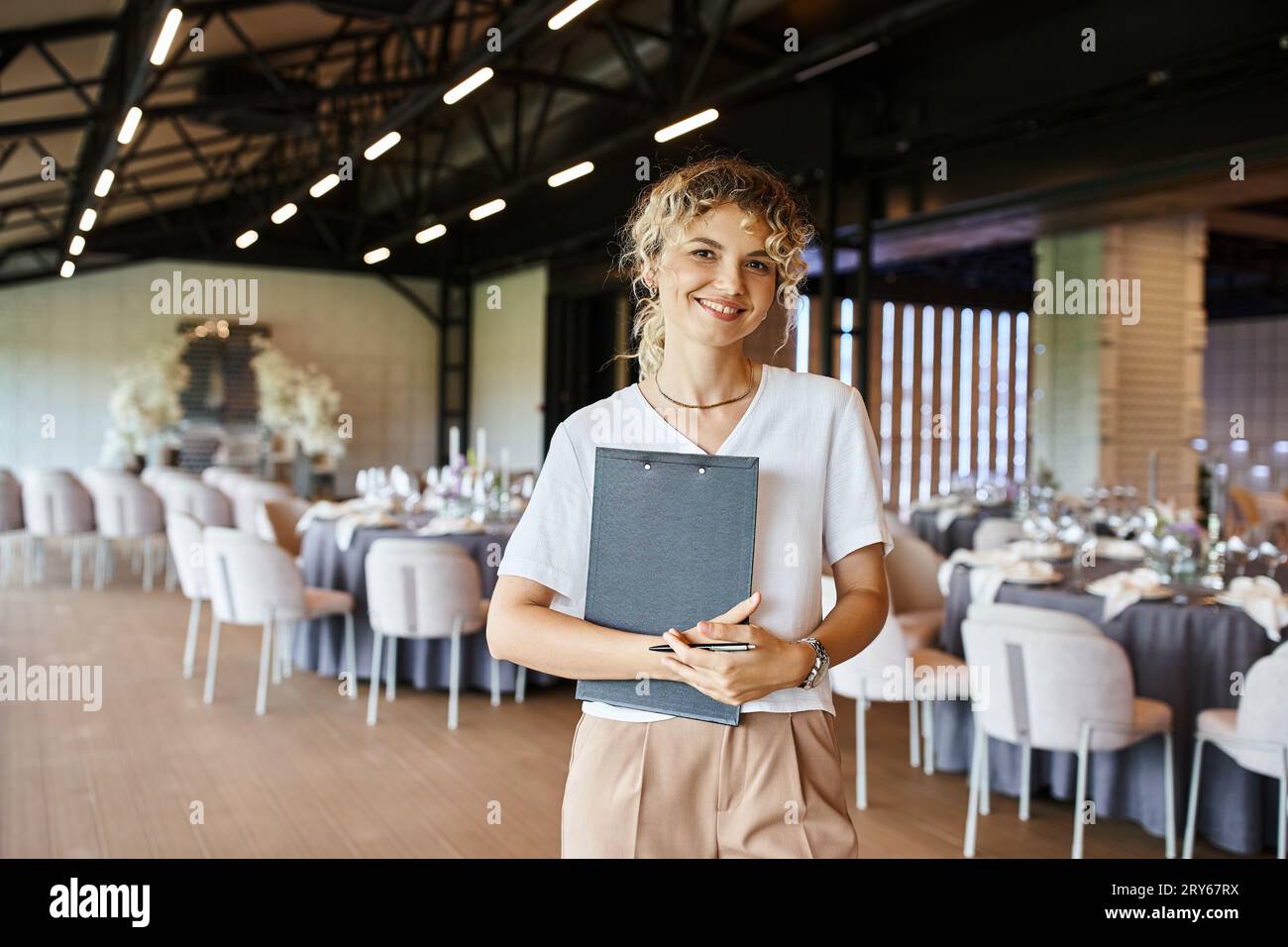 positive decorator with clipboard looking at camera near tables with ...