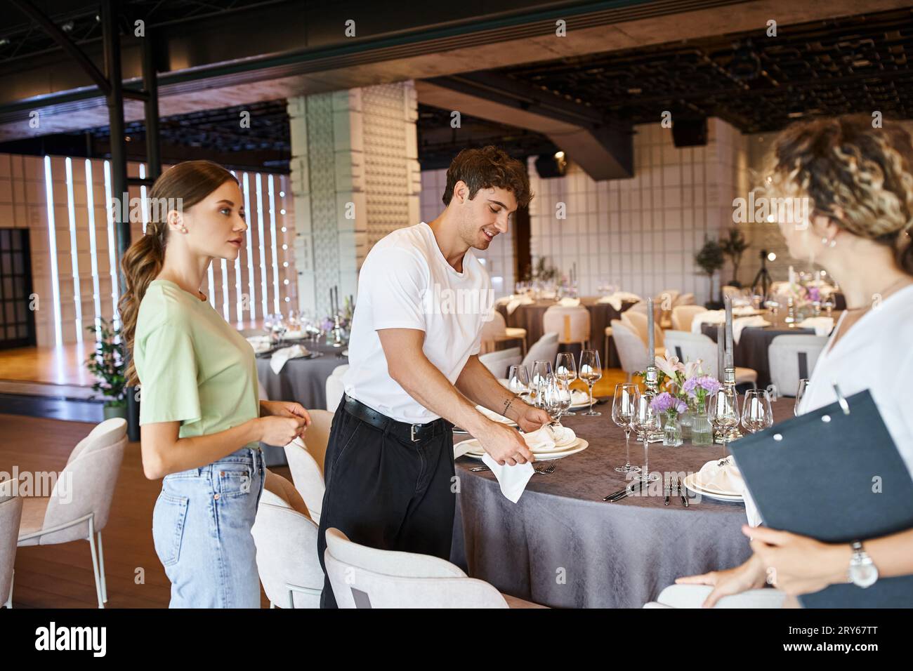 smiling man holding plates near festive table and colleagues in event ...
