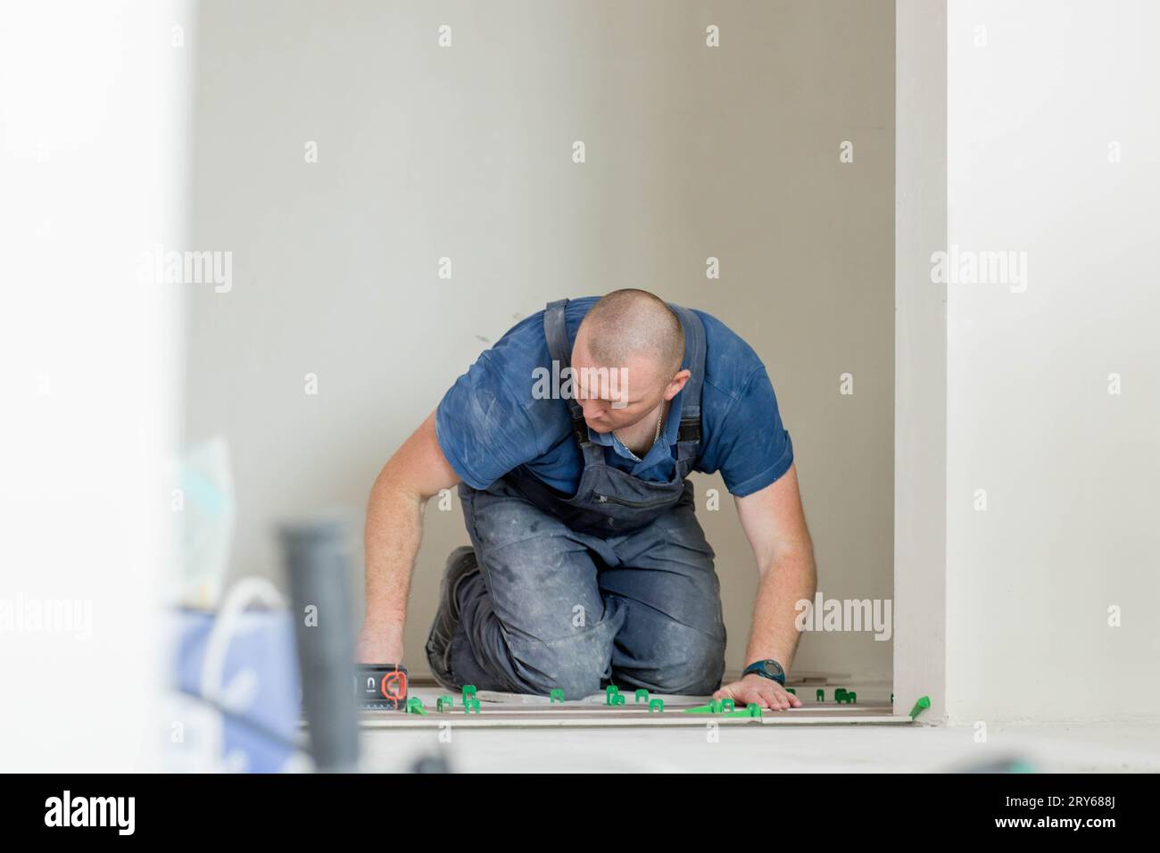 Tiler placing ceramic wall tile in position over adhesive with lash ...