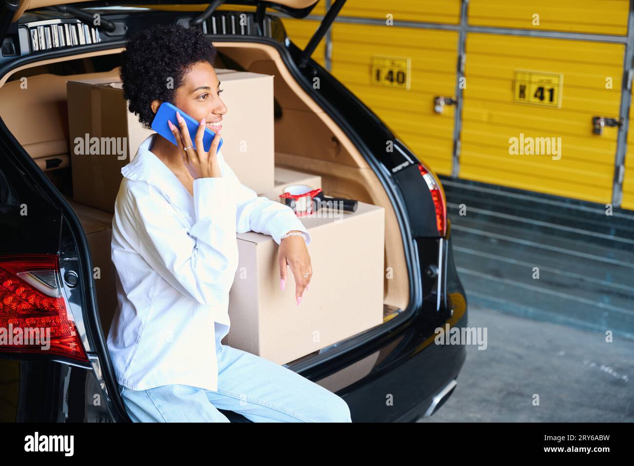 African American woman talking on phone, sitting on edge of trunk Stock ...