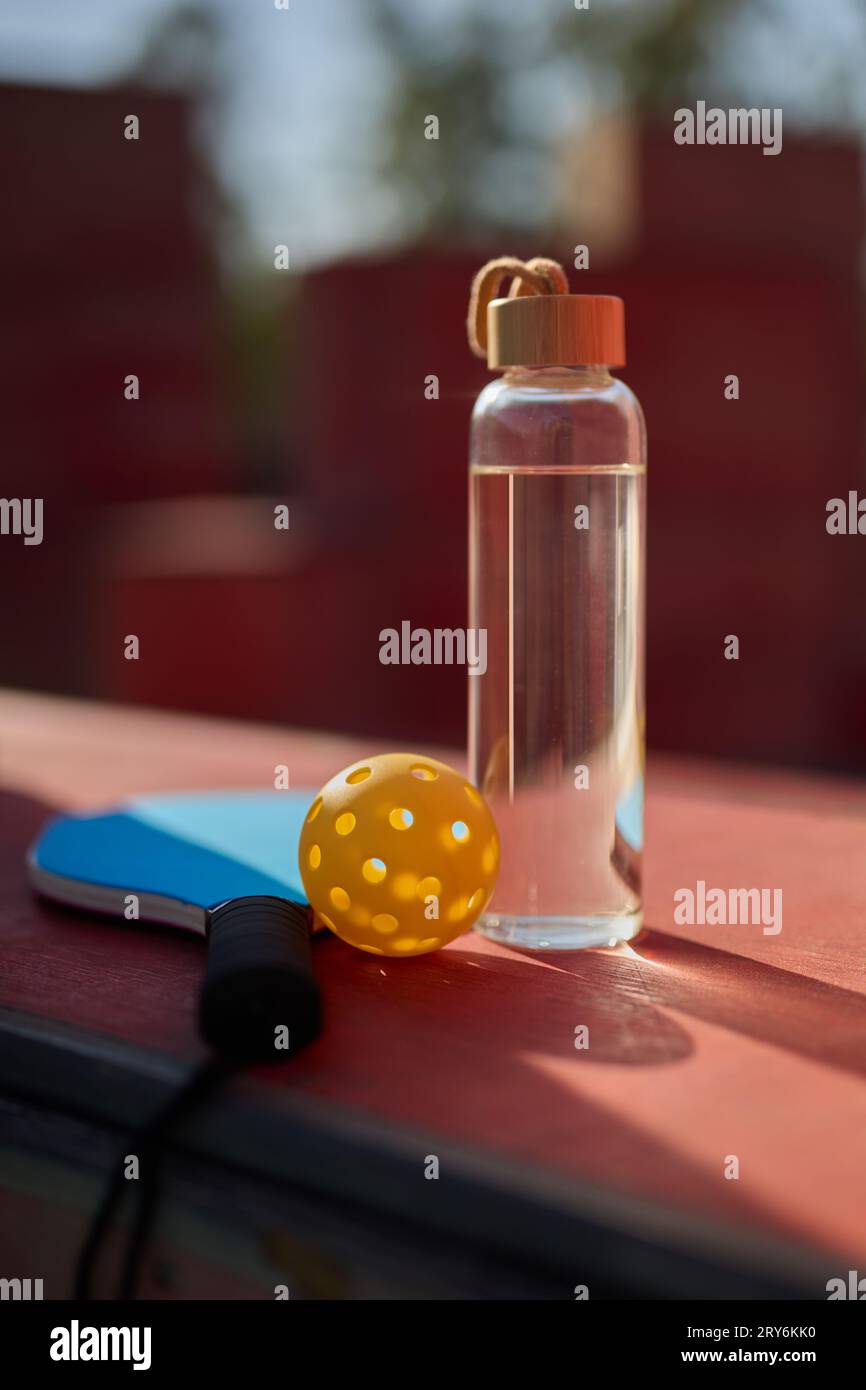 Reusable glass water botle, pickleball paddle and perforated ball on ...
