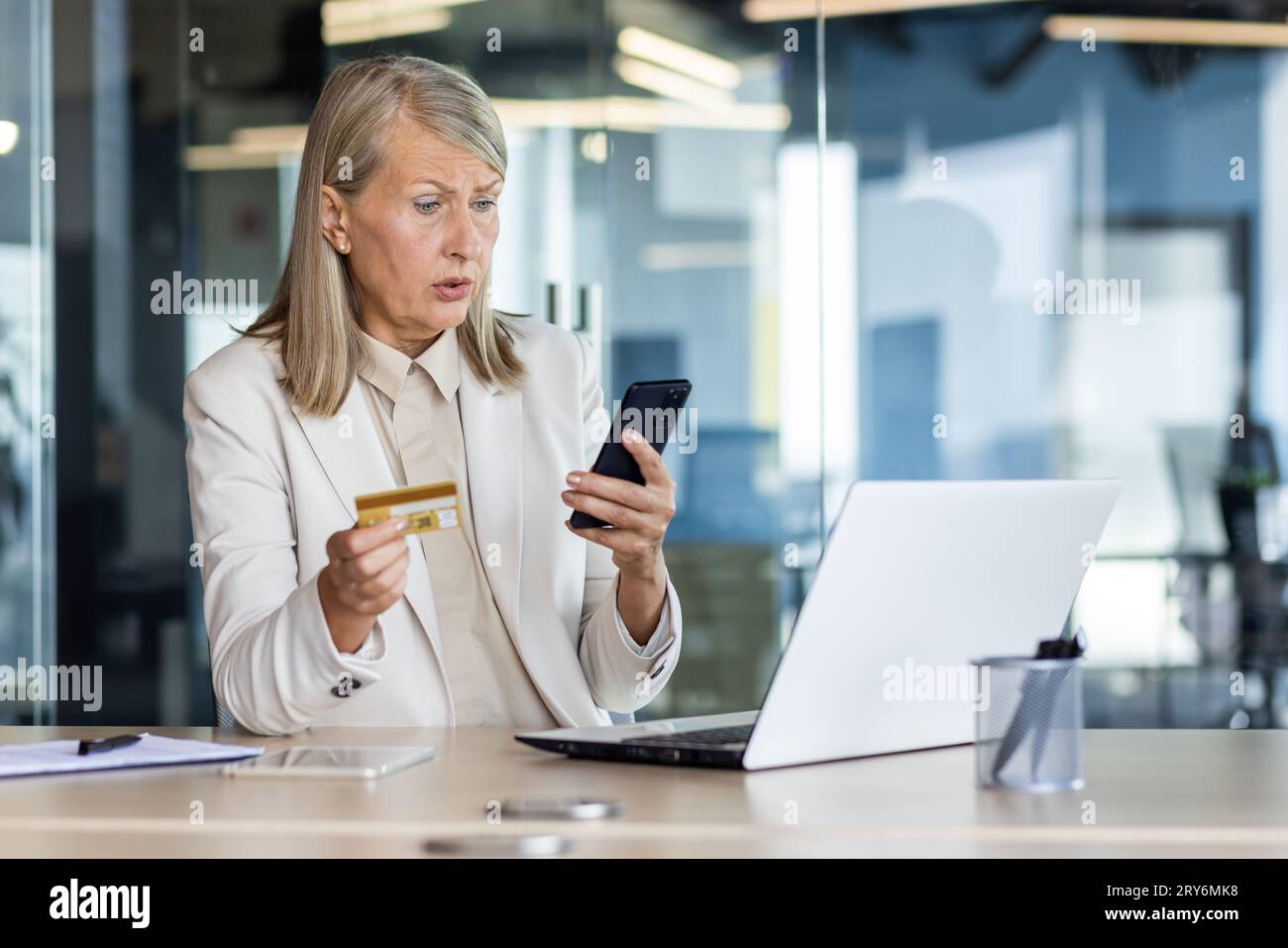 Confused senior businesswoman sitting at the desk in the office in a ...