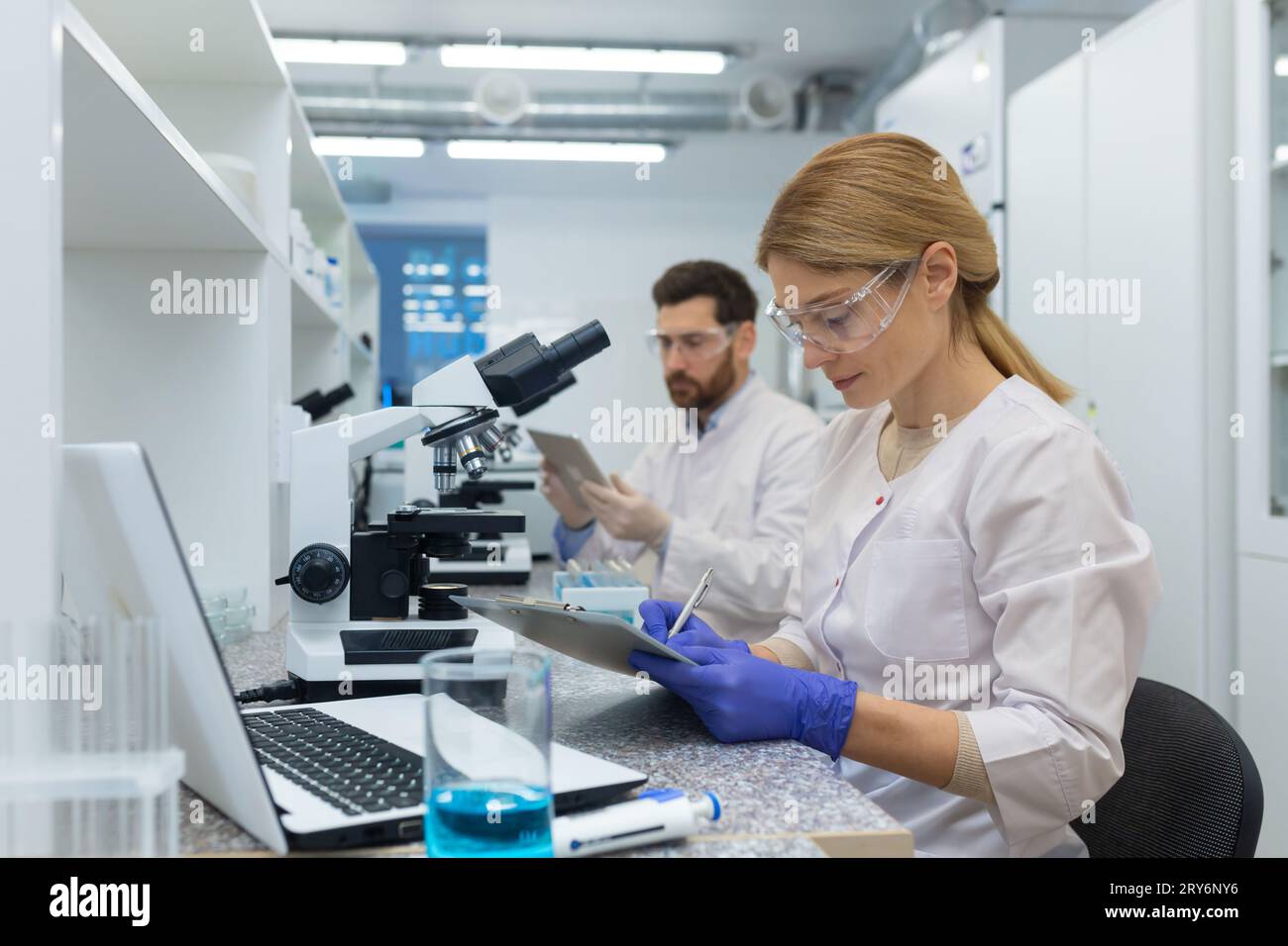 A young female scientist is making research and analysis notes while ...
