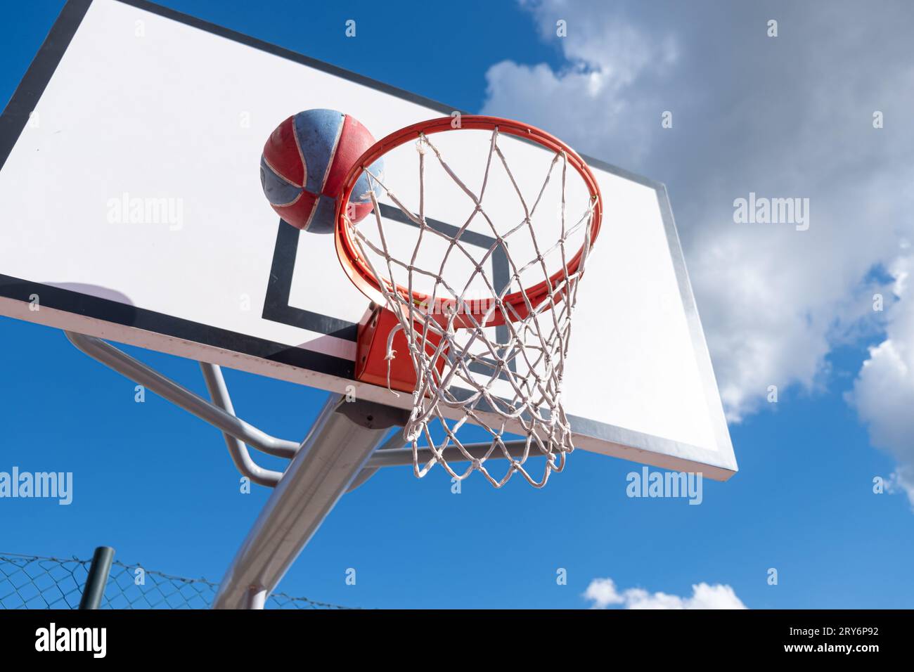 red and blue ball in a basketball hoop with white backboard against a ...