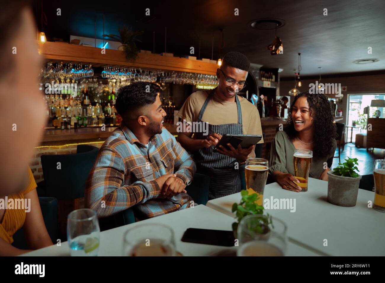 african american male waiter serving group of friends in restaurant ...