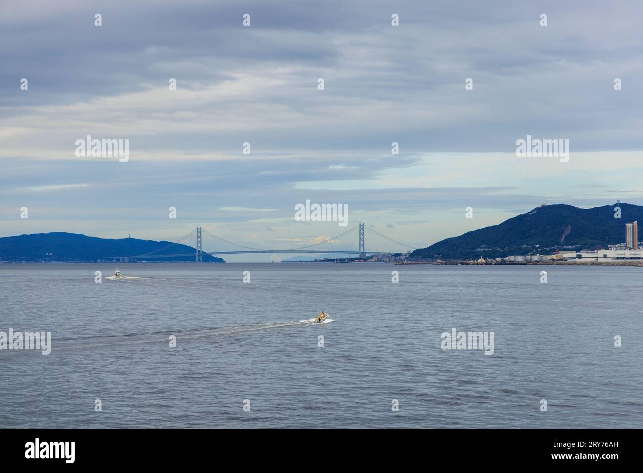 Small boats sail in calm waters near towering suspension bridge Stock ...