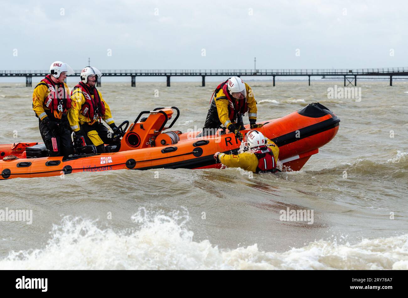 RNLI crew pulling a fellow crewman aboard an inshore lifeboat from a ...