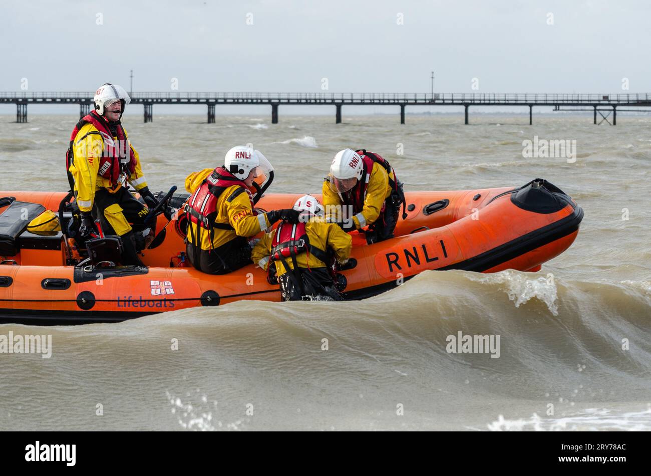 RNLI crew pulling a fellow crewman aboard an inshore lifeboat from a ...