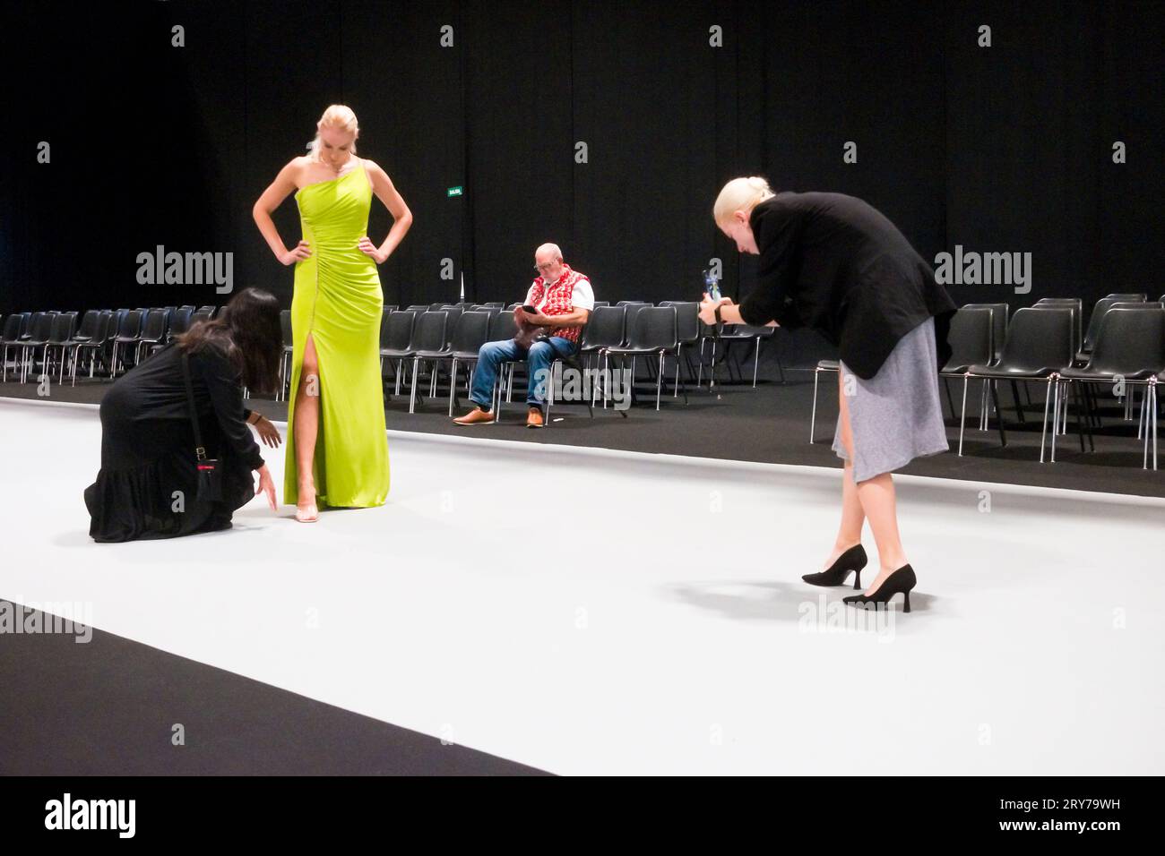 A woman taking photos of a models dressed evening dress on an empty ...