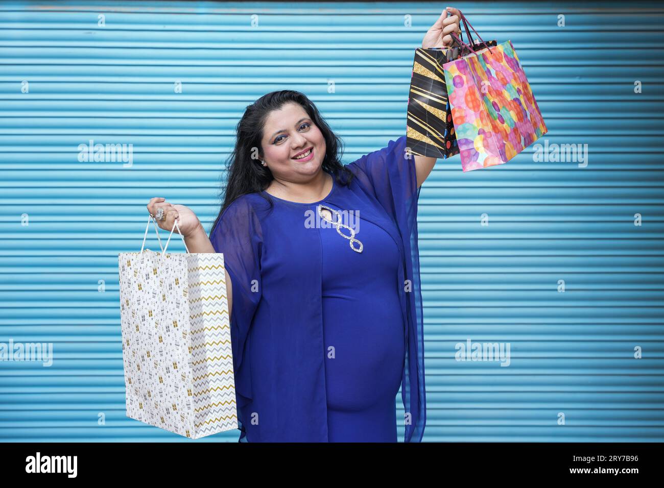 Young cheerful indian plus size woman holding shopping bags isolated ...