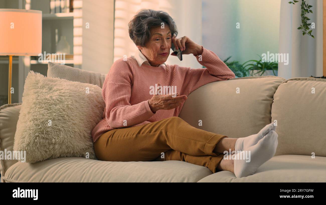 Happy old woman relaxing on cozy sofa talking on smartphone smiling ...