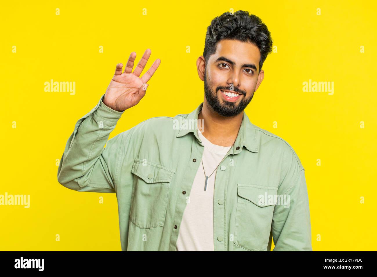 Young Indian man smiling friendly at camera, waving hands gesturing ...