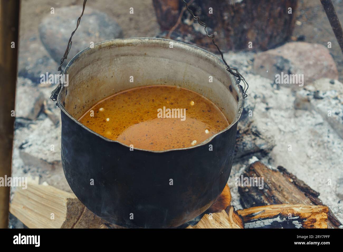 Metal vessel with spicy and mouthwatering soup hanging on tripod under ...