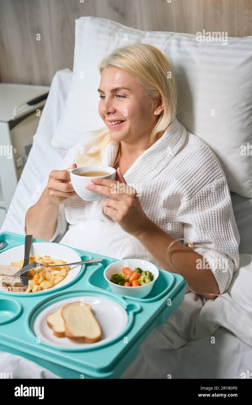 Recovering female patient in hospital gown is having breakfast in bed ...