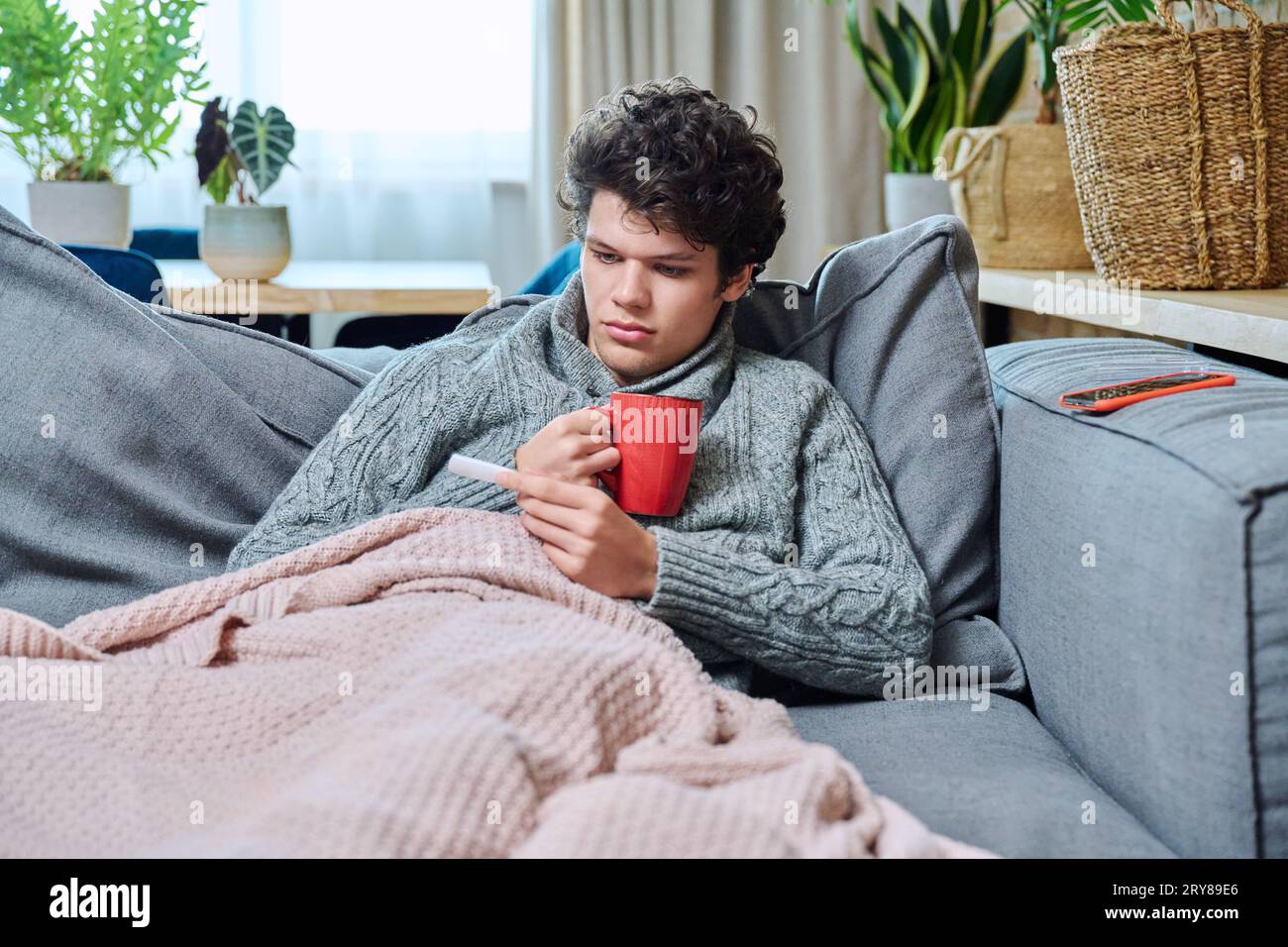 Young guy checking temperature, lying on couch under blanket Stock ...