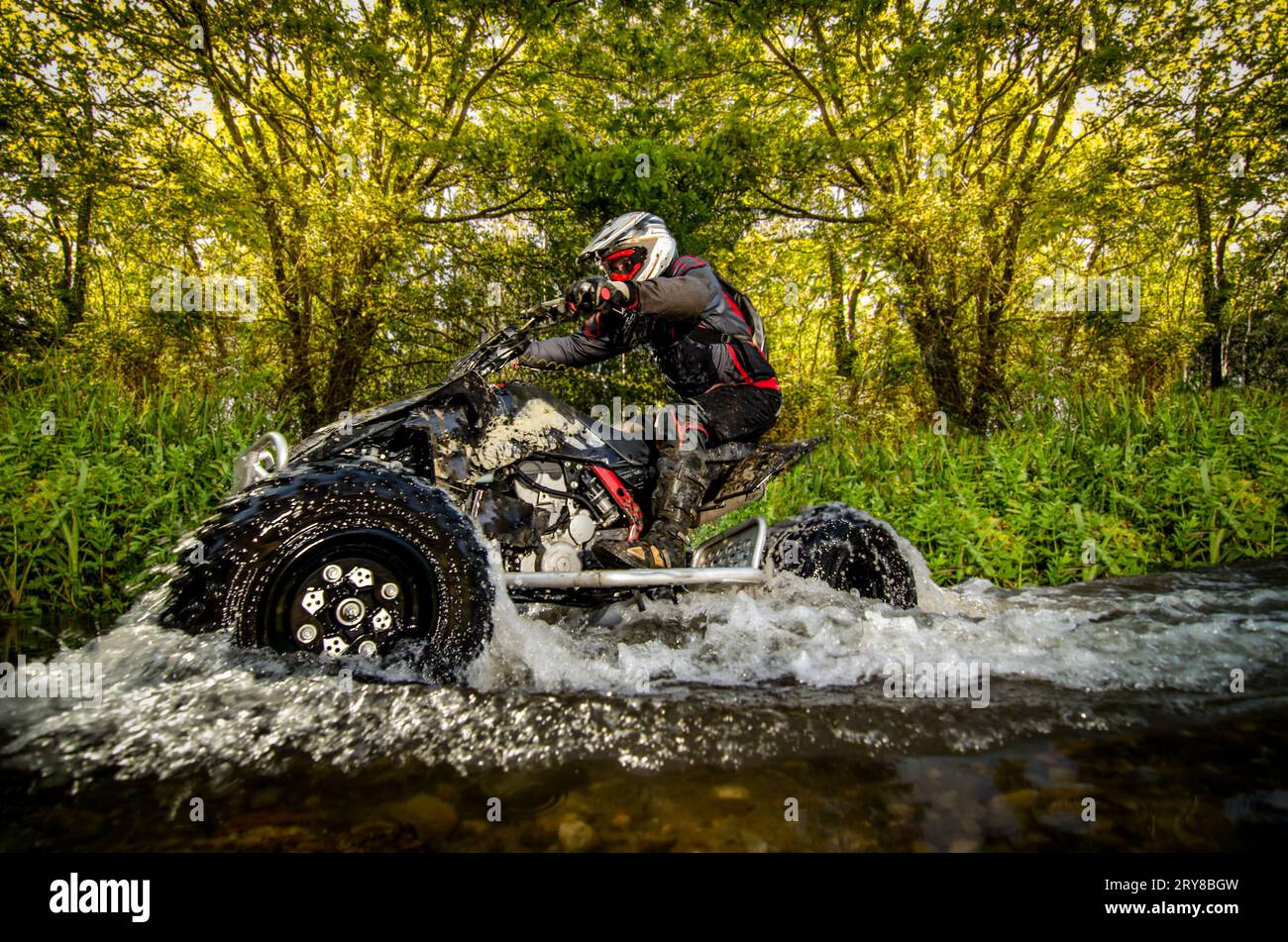 Quad rider through water stream Stock Photo - Alamy