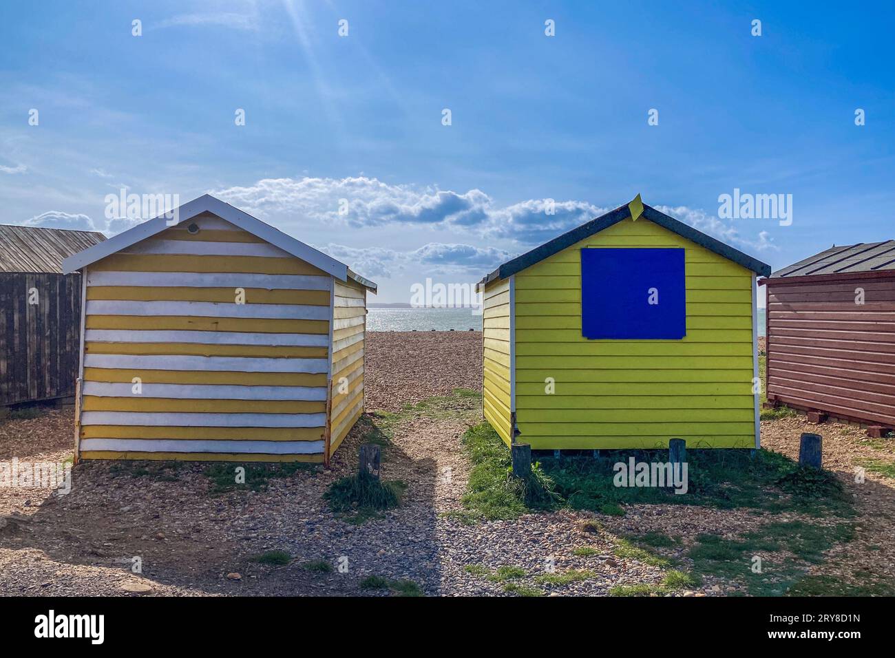 Colourful yellow beach huts stand in a row at the beach. One yellow hut ...