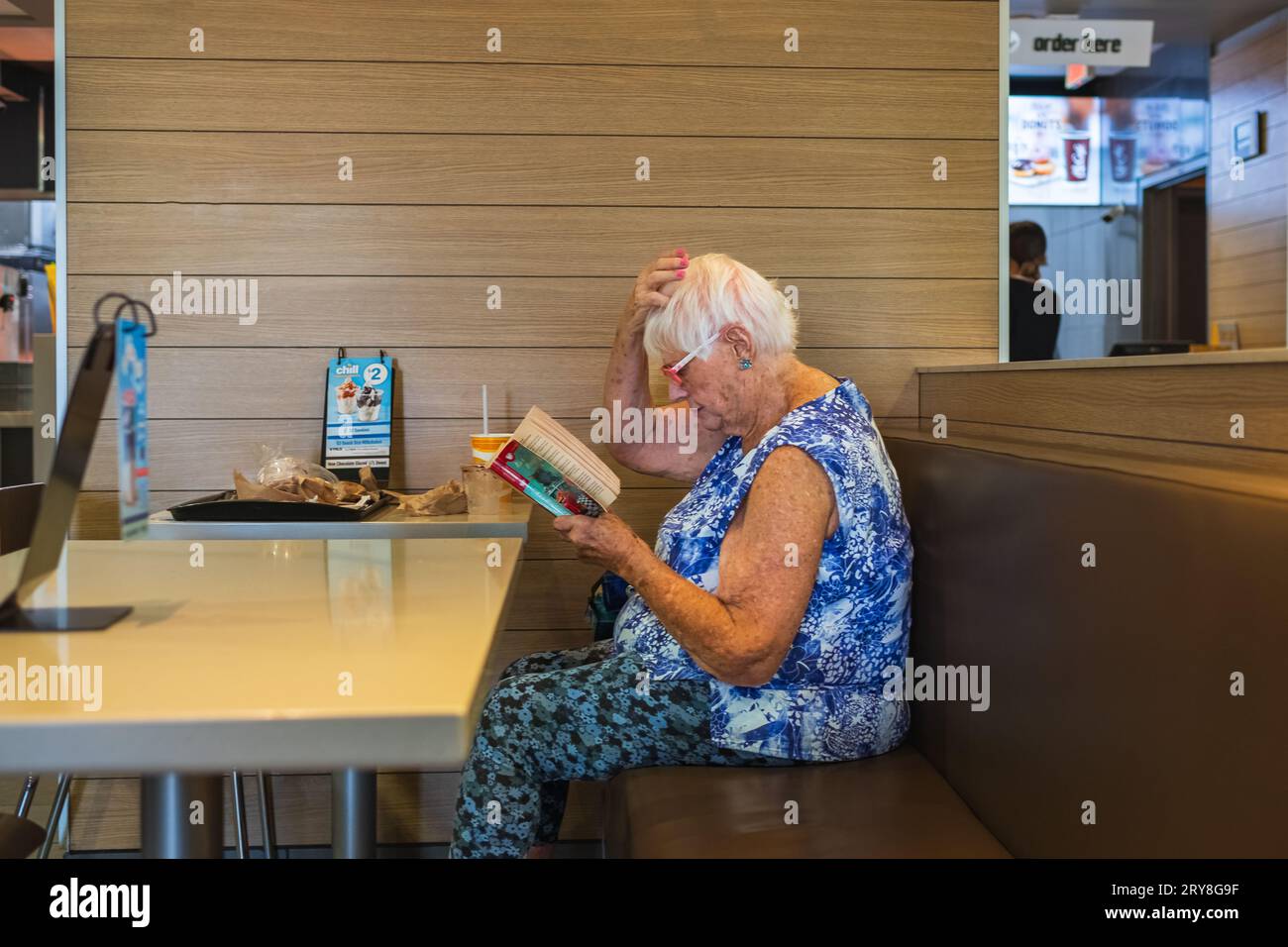 Side photo of elderly pensioner woman reading a book at cafe. Old lady ...
