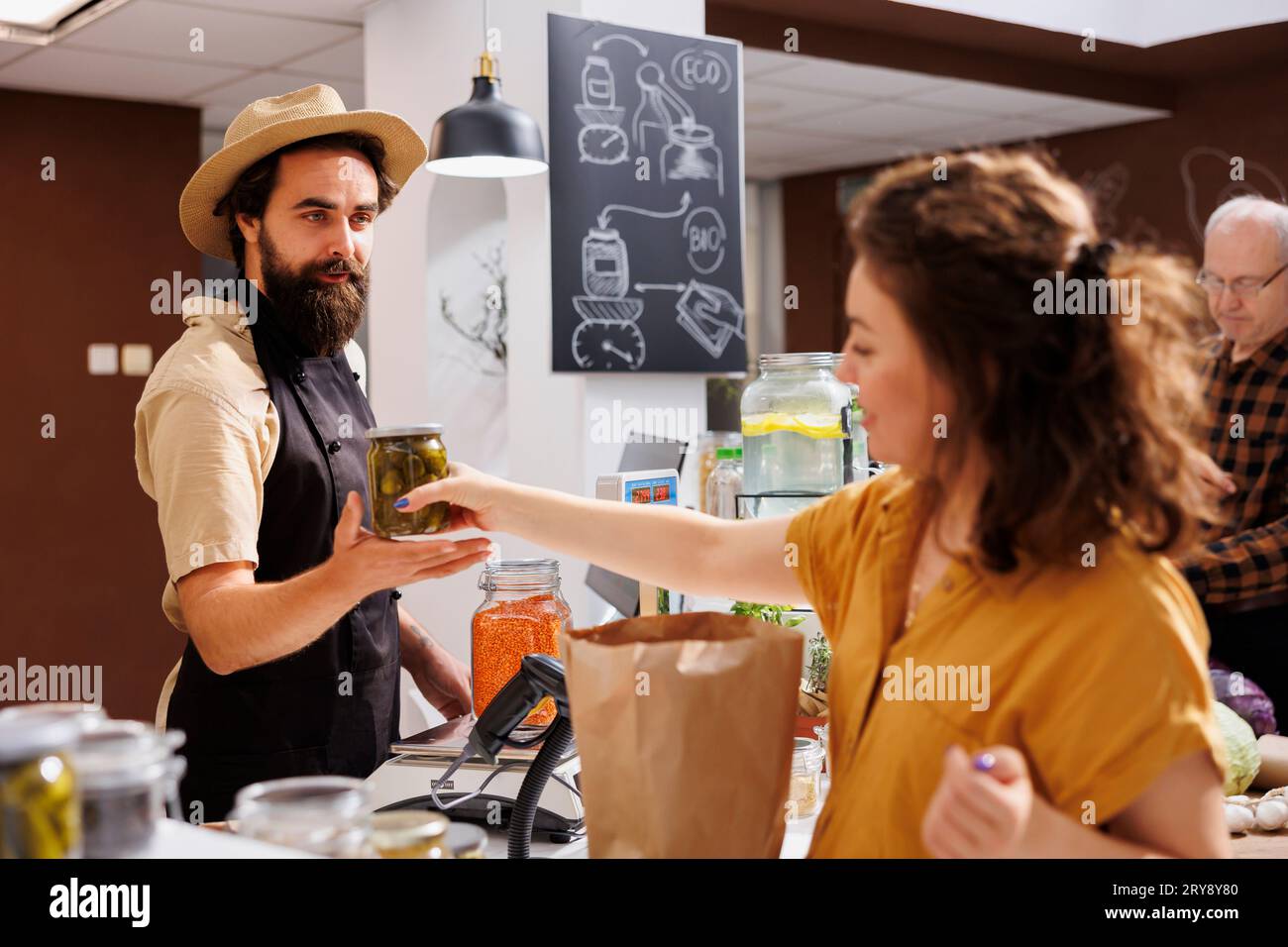 Cheerful merchant at checkout counter in zero waste shop selling vegan ...
