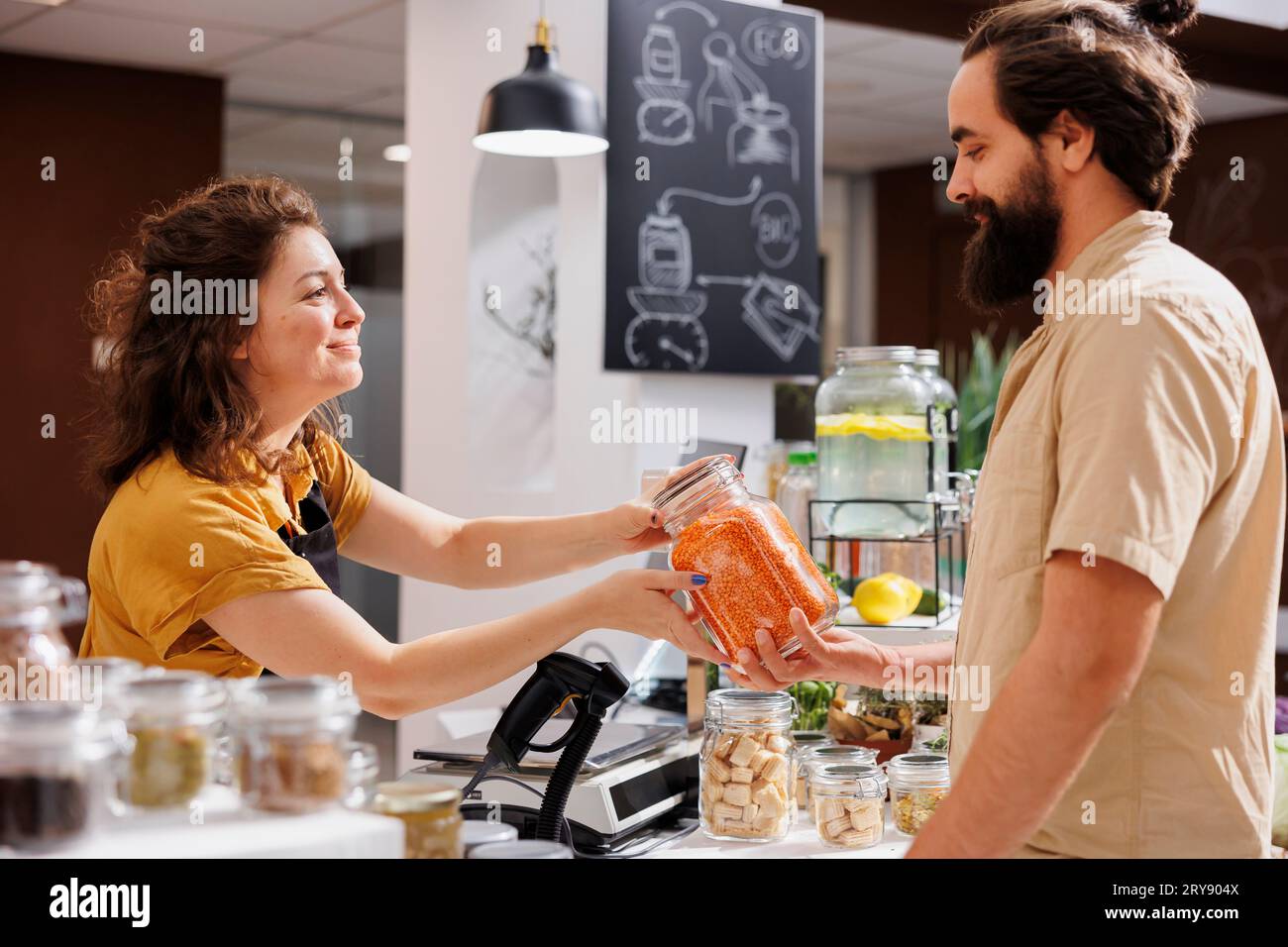 Vendor at zero waste supermarket checkout counter weighting food jar ...