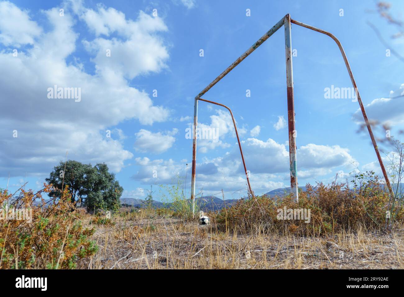 Old rusty soccer goal in an overgrown field with a broken soccer ball ...