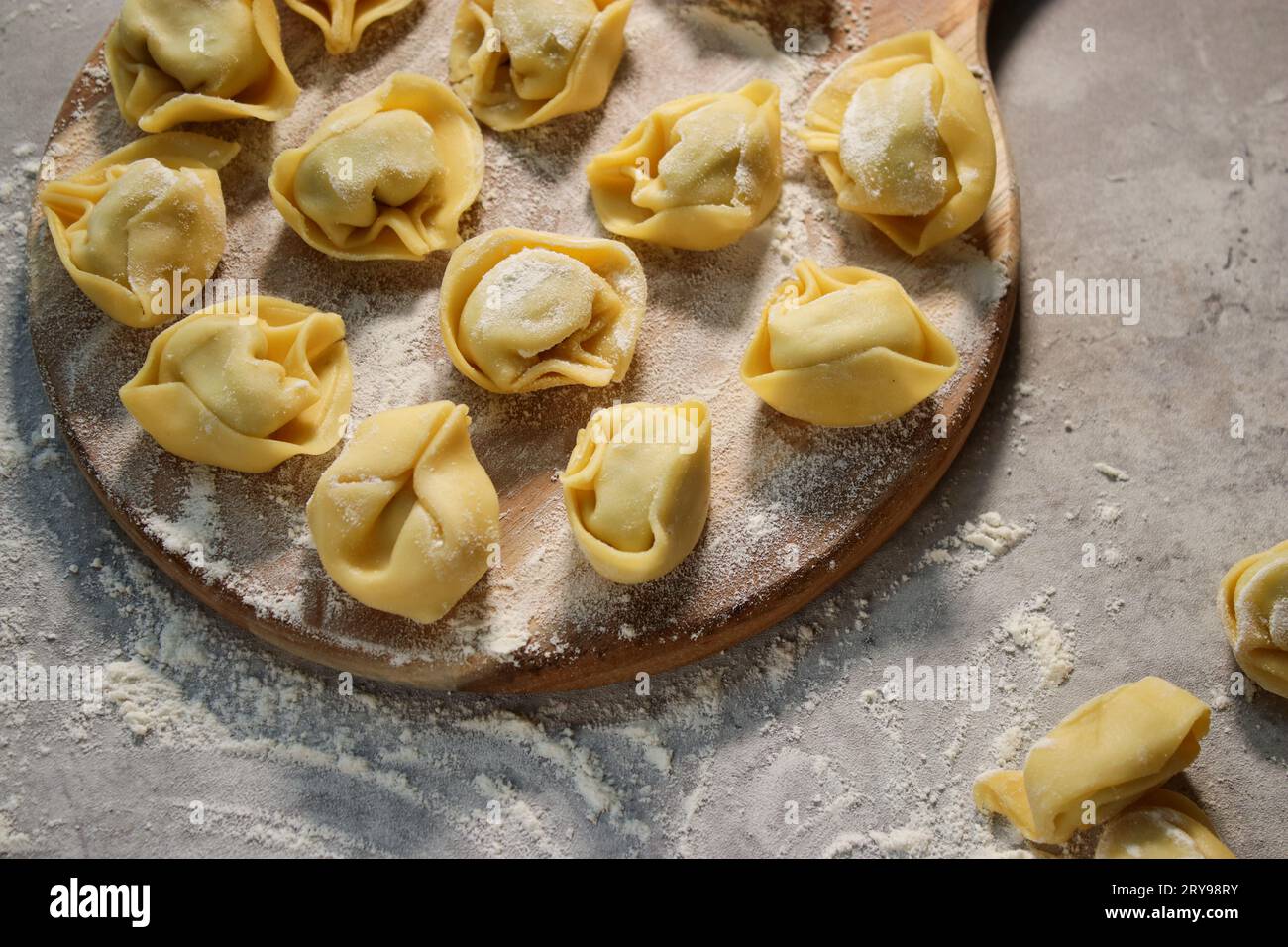 Raw traditional ravioli tortellini on wooden plate, grey table with ...