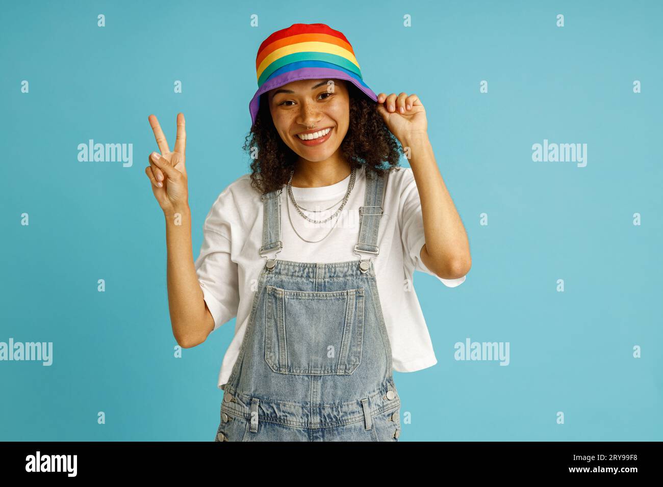 Woman in rainbow cap over blue background smiling with happy face doing ...