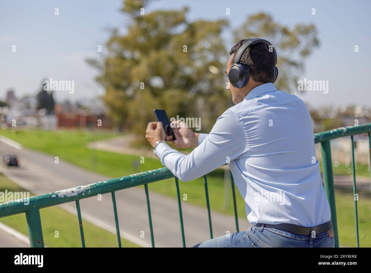 Man in shirt with headphones using his mobile phone leaning on the ...