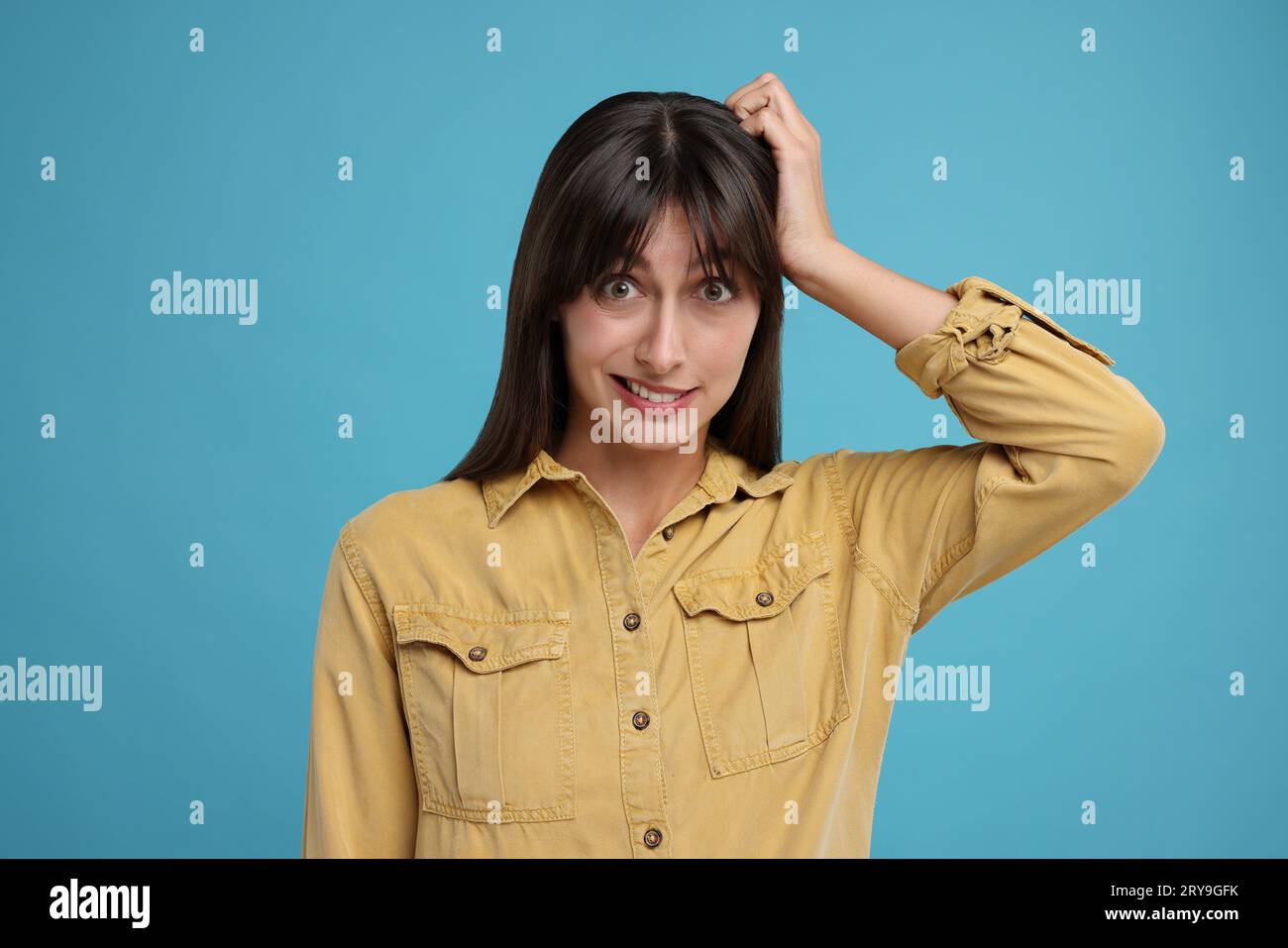 Embarrassed woman scratching head on light blue background Stock Photo ...