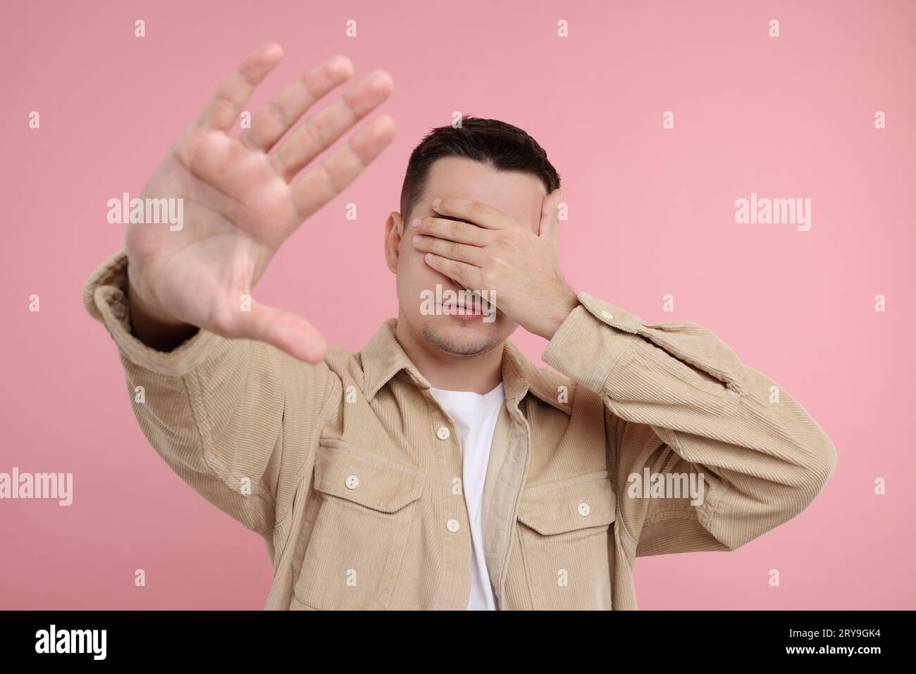 Embarrassed man covering face with hand on pink background Stock Photo ...