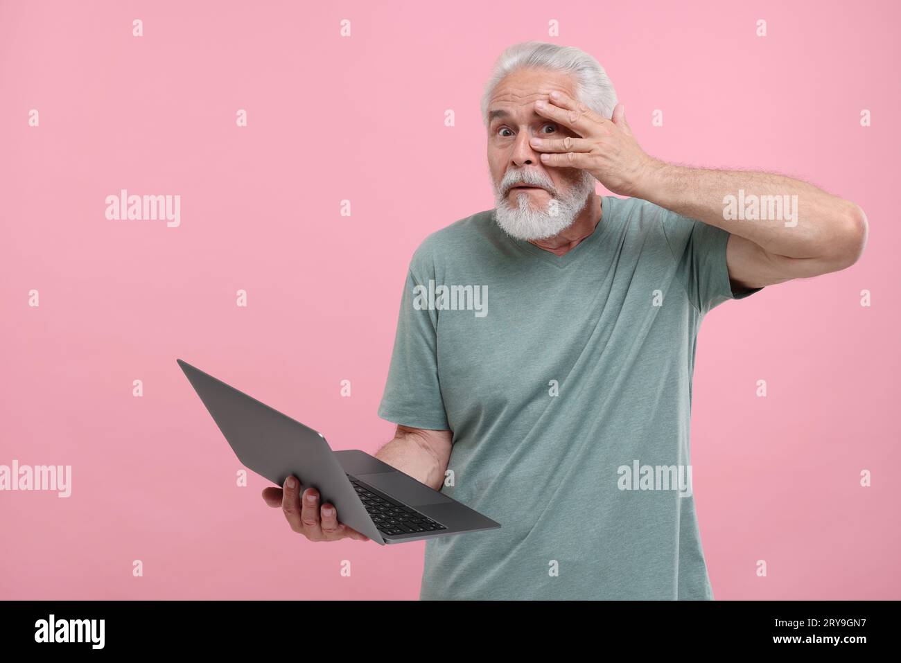Embarrassed senior man holding laptop on pink background. Space for ...